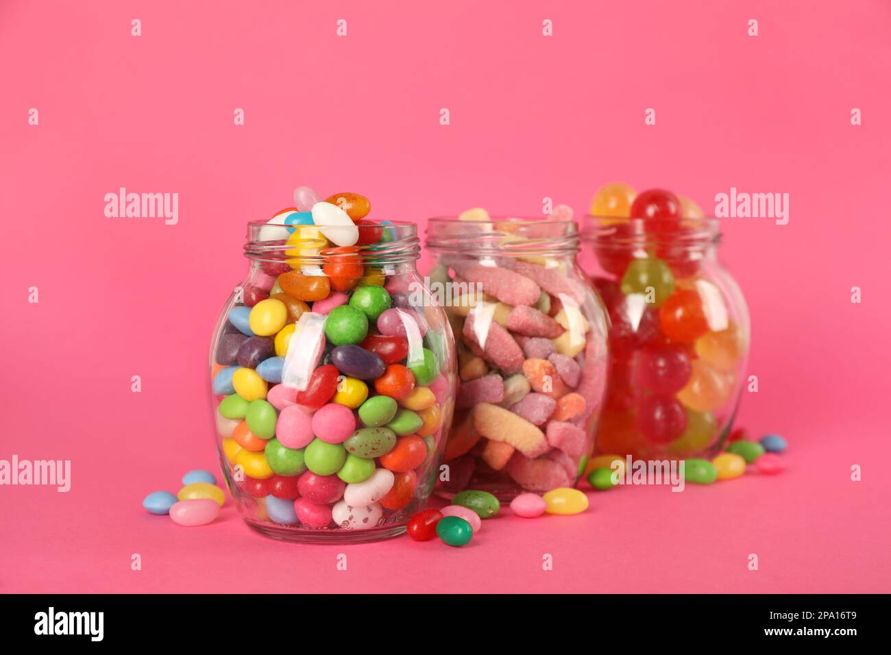 Glass jars with lots of different candies on bright pink background ...