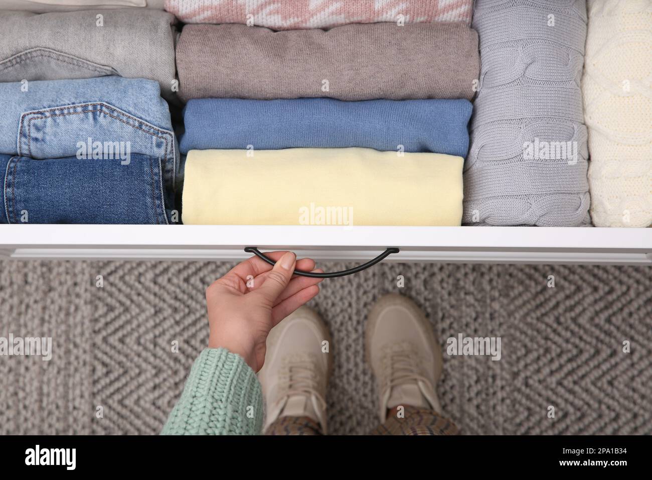 Woman opening drawer with folded clothes indoors, top view. Vertical ...