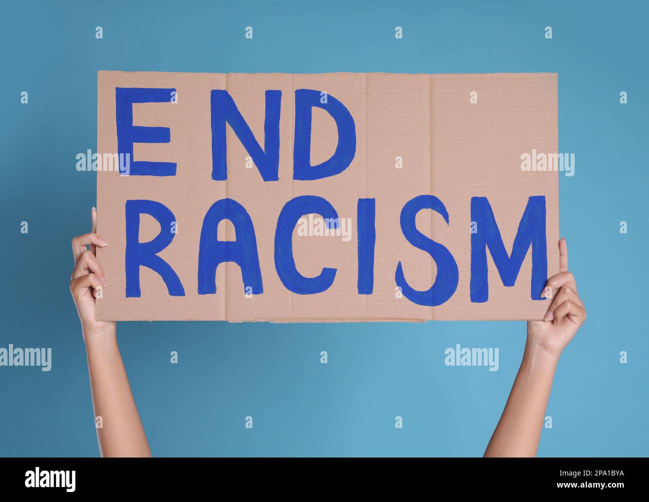 Woman holding sign with phrase End Racism on light blue background ...