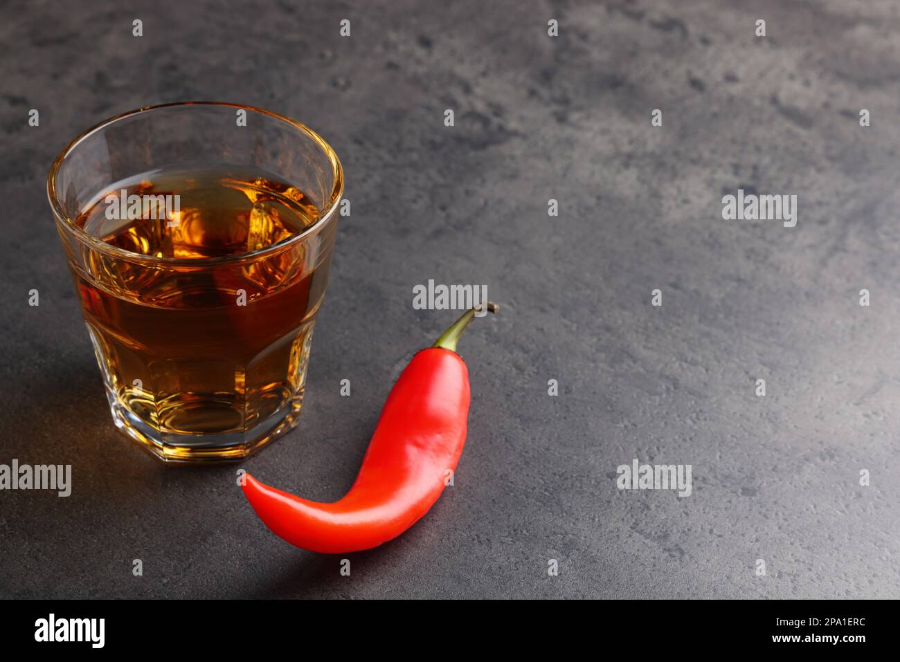 Red hot chili pepper and vodka in glass on grey table, space for text ...