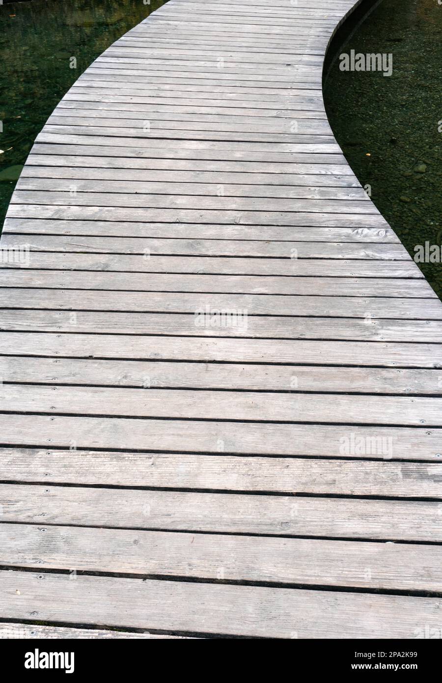 Long and winding wooden boardwalk pier over a clear dark blue mountain ...