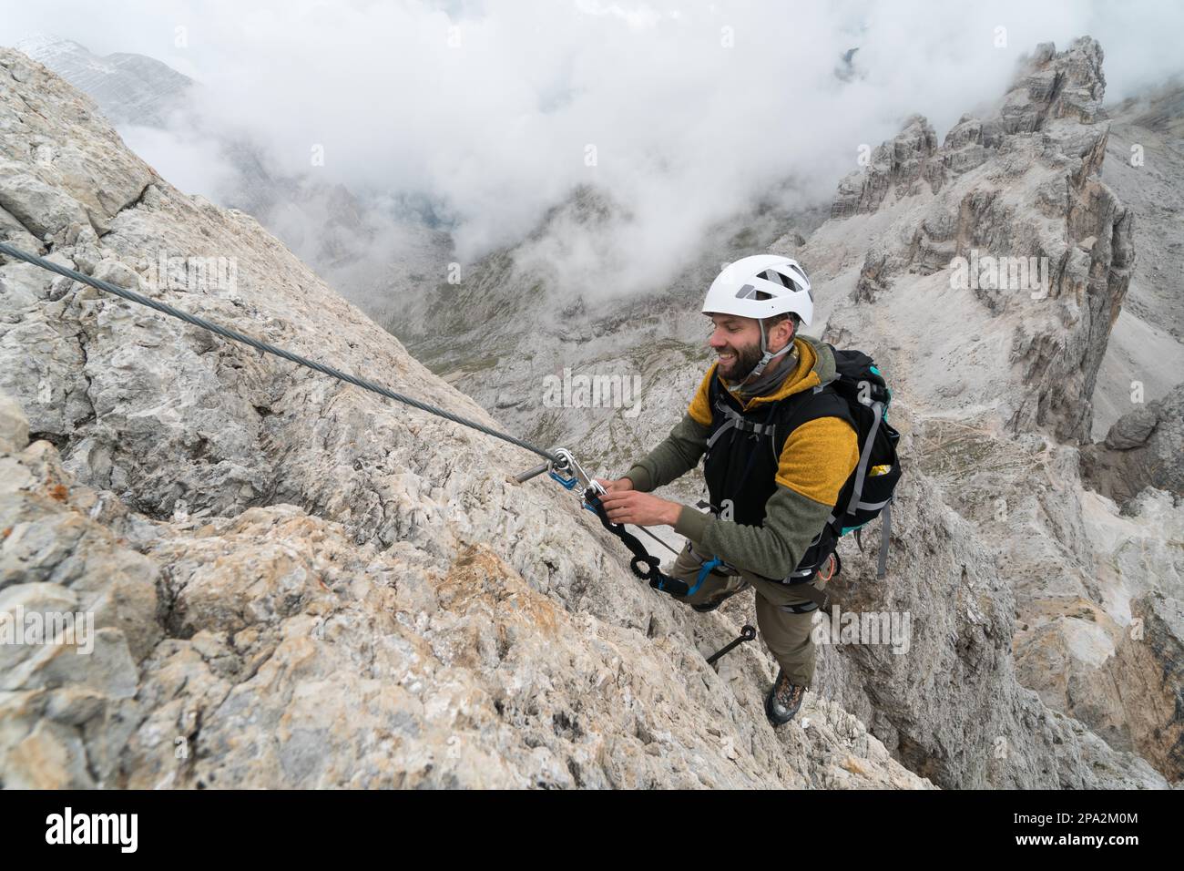 Young handsome male climber on a steep and exposed rock face climbs a ...