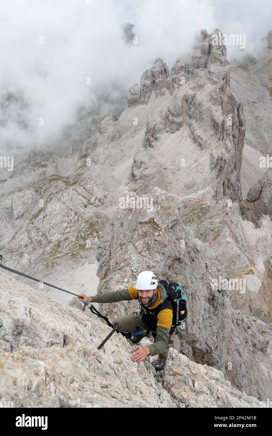 Young handsome male climber on a steep and exposed rock face climbs a ...
