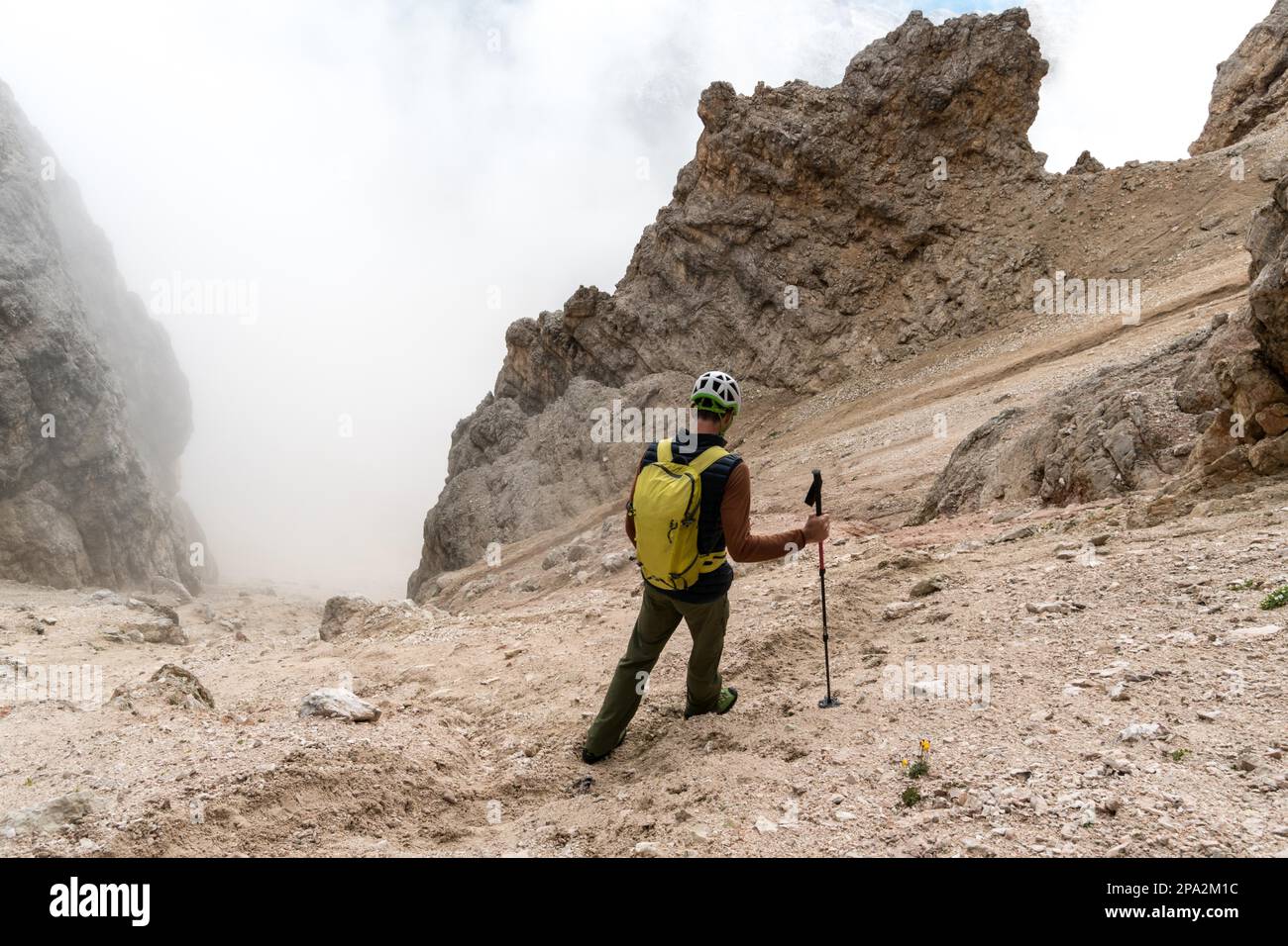 Tall male mountain climber hiking down a steep scree and rock slope in ...