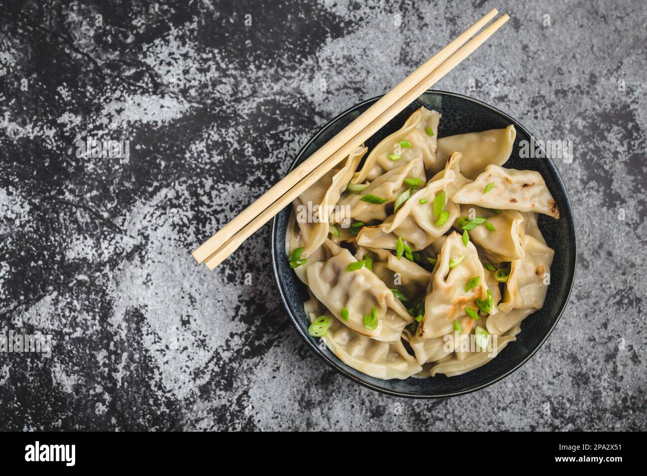 Asian dumplings in bowl, chopsticks, rustic stone background. Top view ...