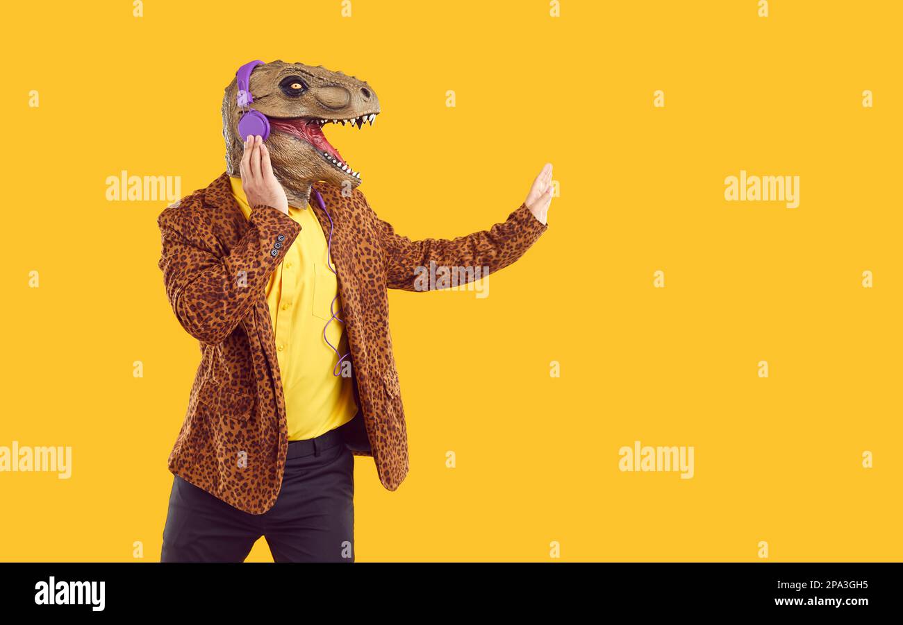 Eccentric funny showman in rubber dinosaur mask listening music in ...
