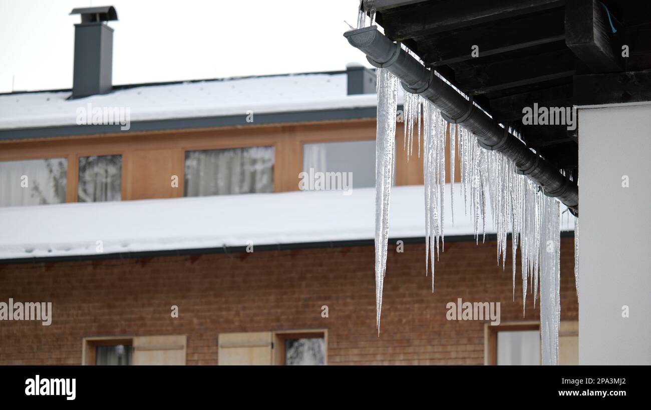 Icicles hanging from gutter in background house with window and chimney ...