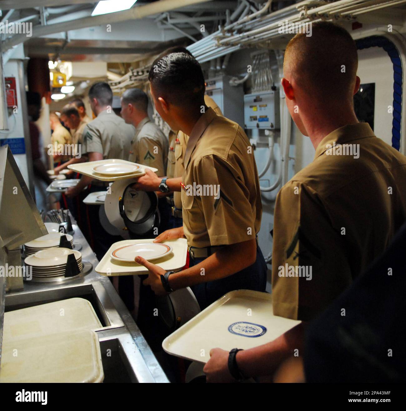 U.S. Marines hold plates and trays bearing the emblem of the USS ...