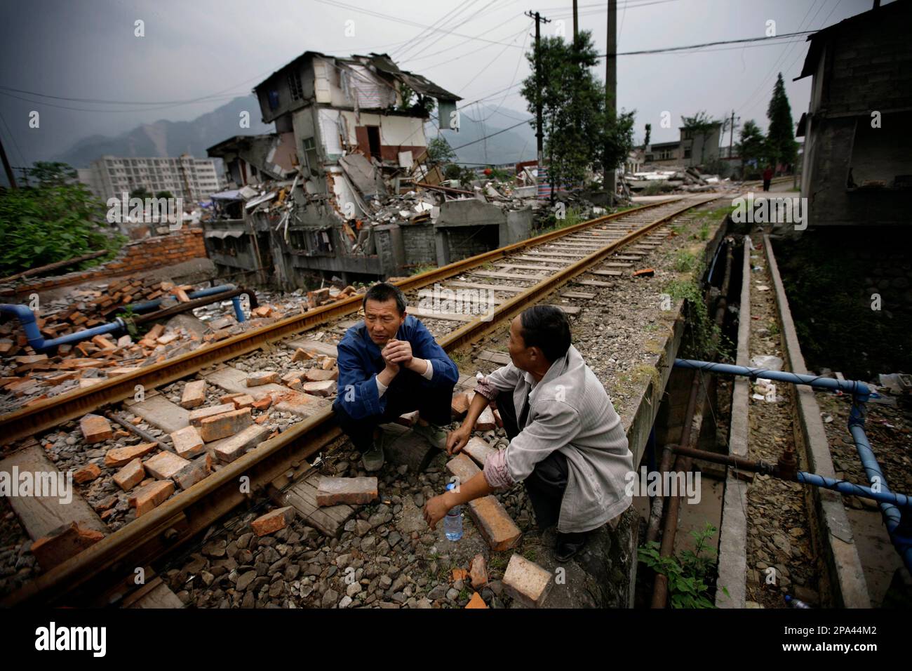 Earthquake survivors sit beside a railway track between collapsed ...
