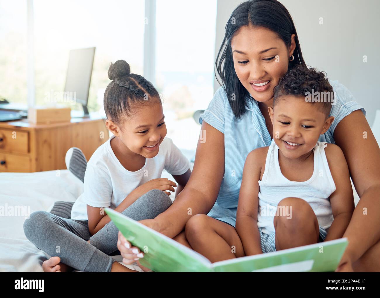 Mother reading a book to her children in a bedroom to relax, bond and ...
