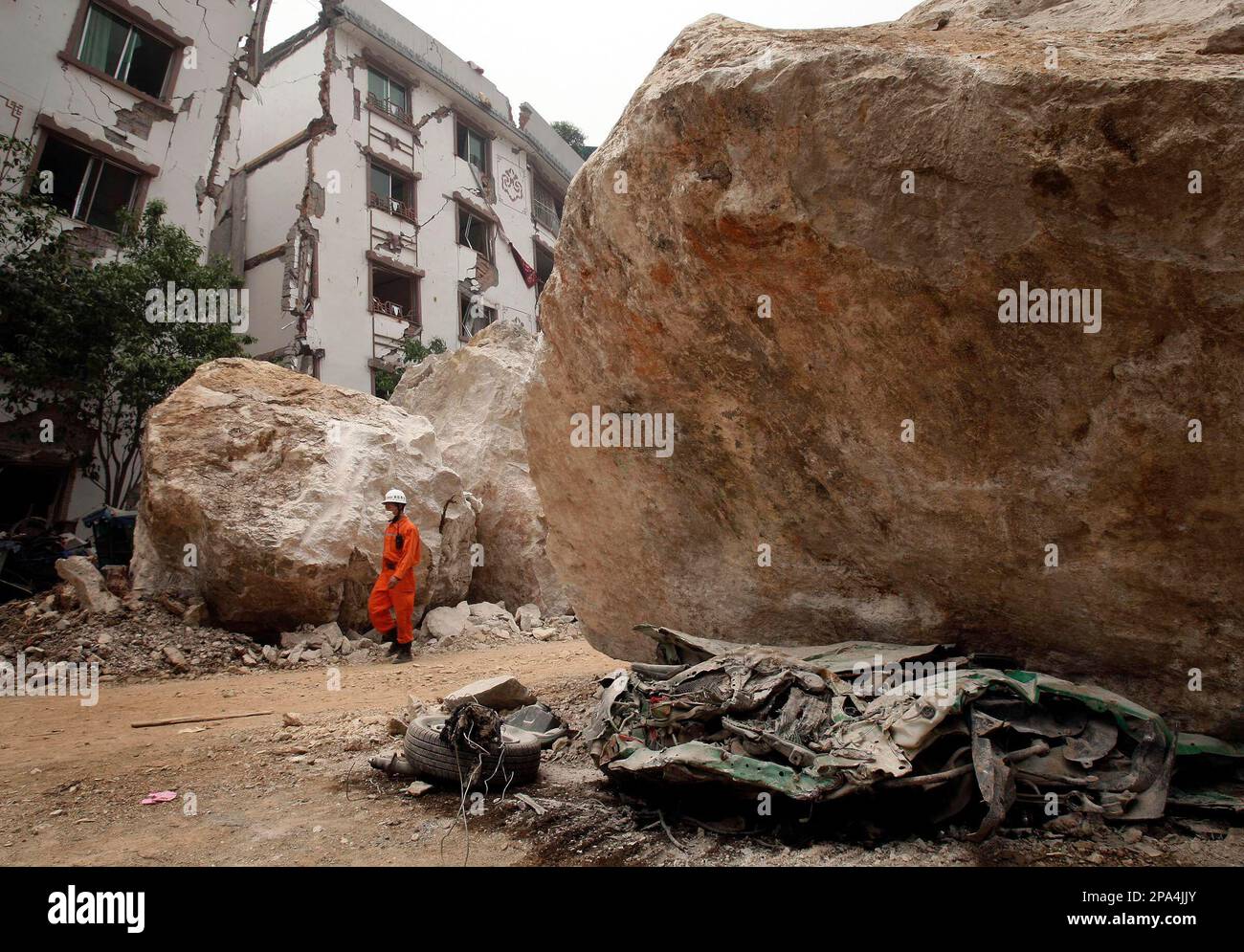 A rescuer walks past a giant rock which has flattened a car next to ...