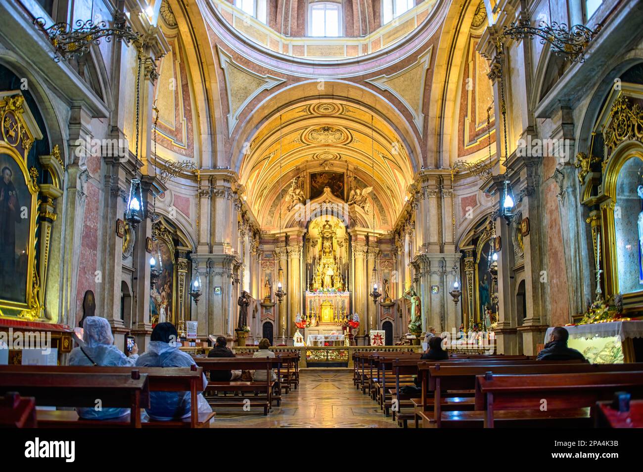 People sit in the symmetric view of benches inside of the Catholic temple. The altar and part of ...