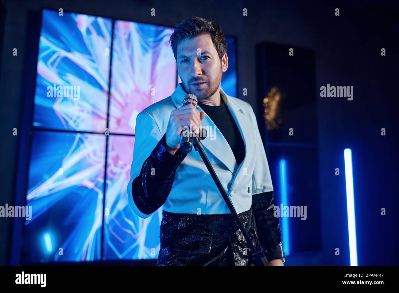 Portrait of handsome attractive singer singing in microphone on stage ...