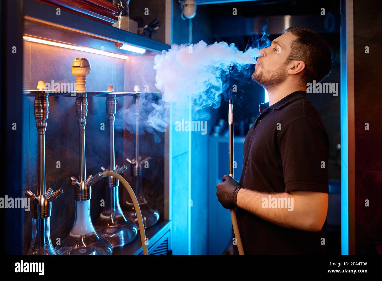 Young man smoking at hookah bar while preparing equipment for client ...