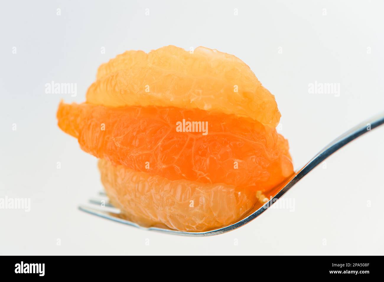 Different coloured grapefruit segments balanced on a fork against a ...