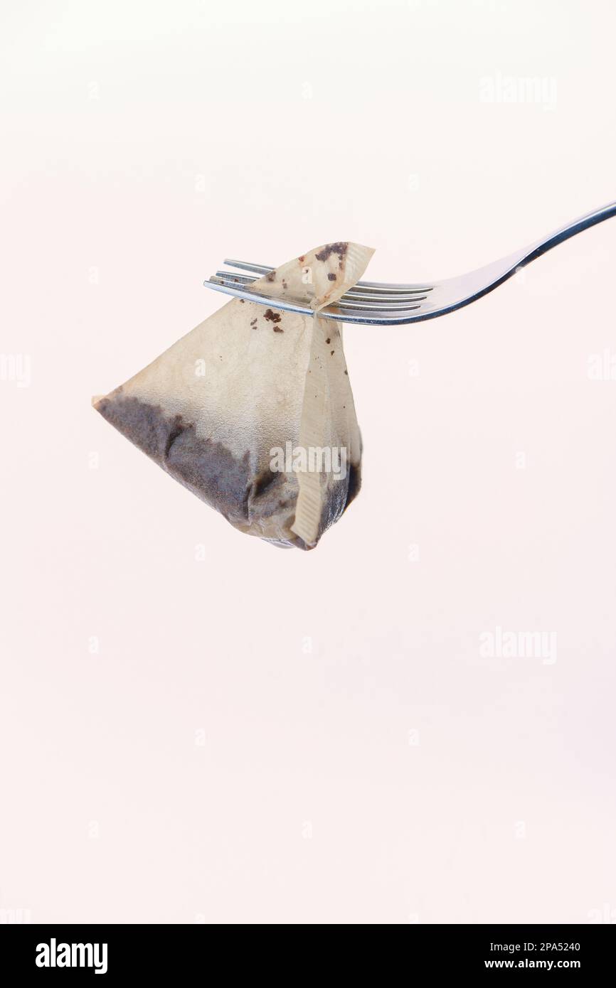 Used triangle tea Bag hanging from a fork against a white background ...