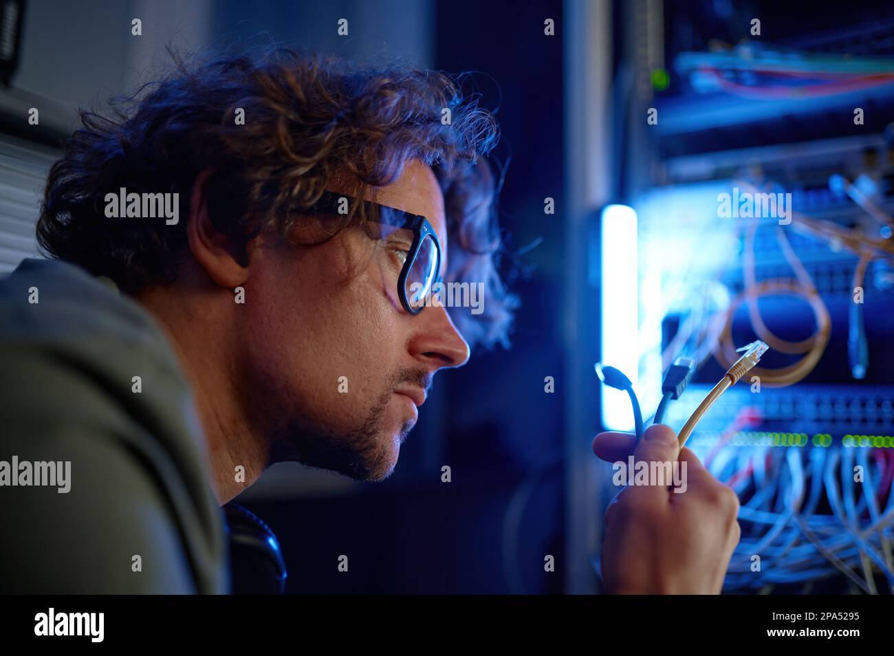Closeup face of male network engineer connecting cables in server room ...