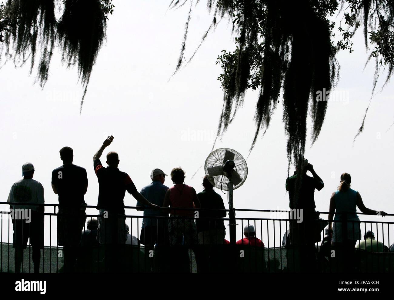 Spectators take advantage of a fan and trees to stay cool while ...