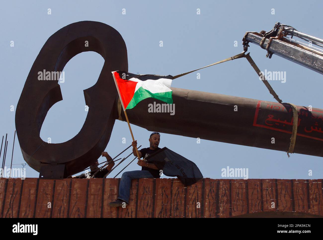 A man waves a Palestinian flag in front of a nine-meter metal key ...