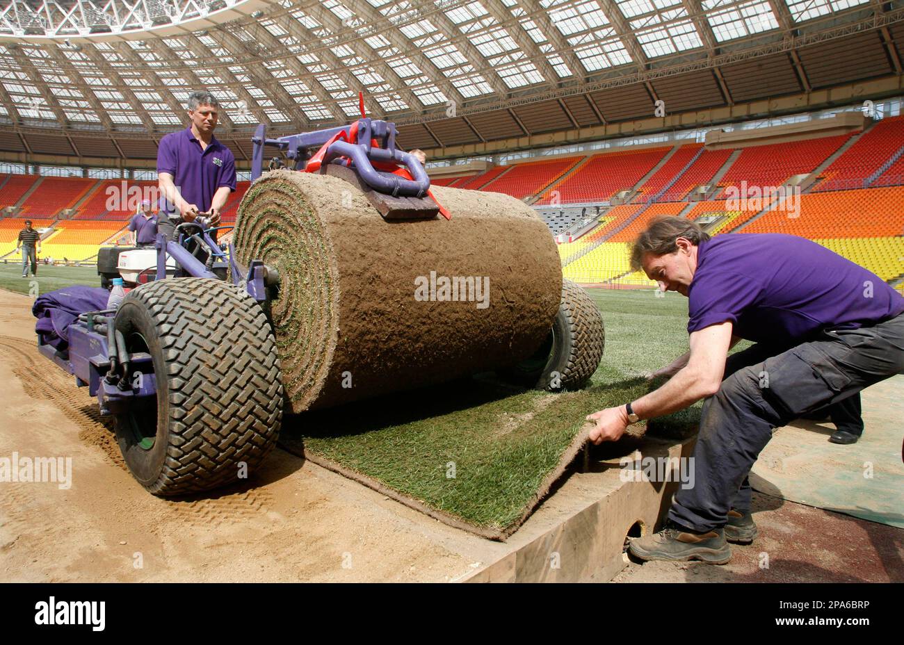 Workers place pieces of turf to cover the artificial grass soccer field ...