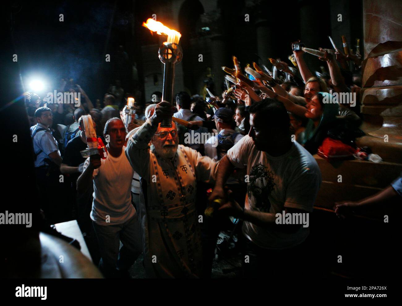 A Greek Orthodox priest runs with a torch to light the candles of ...