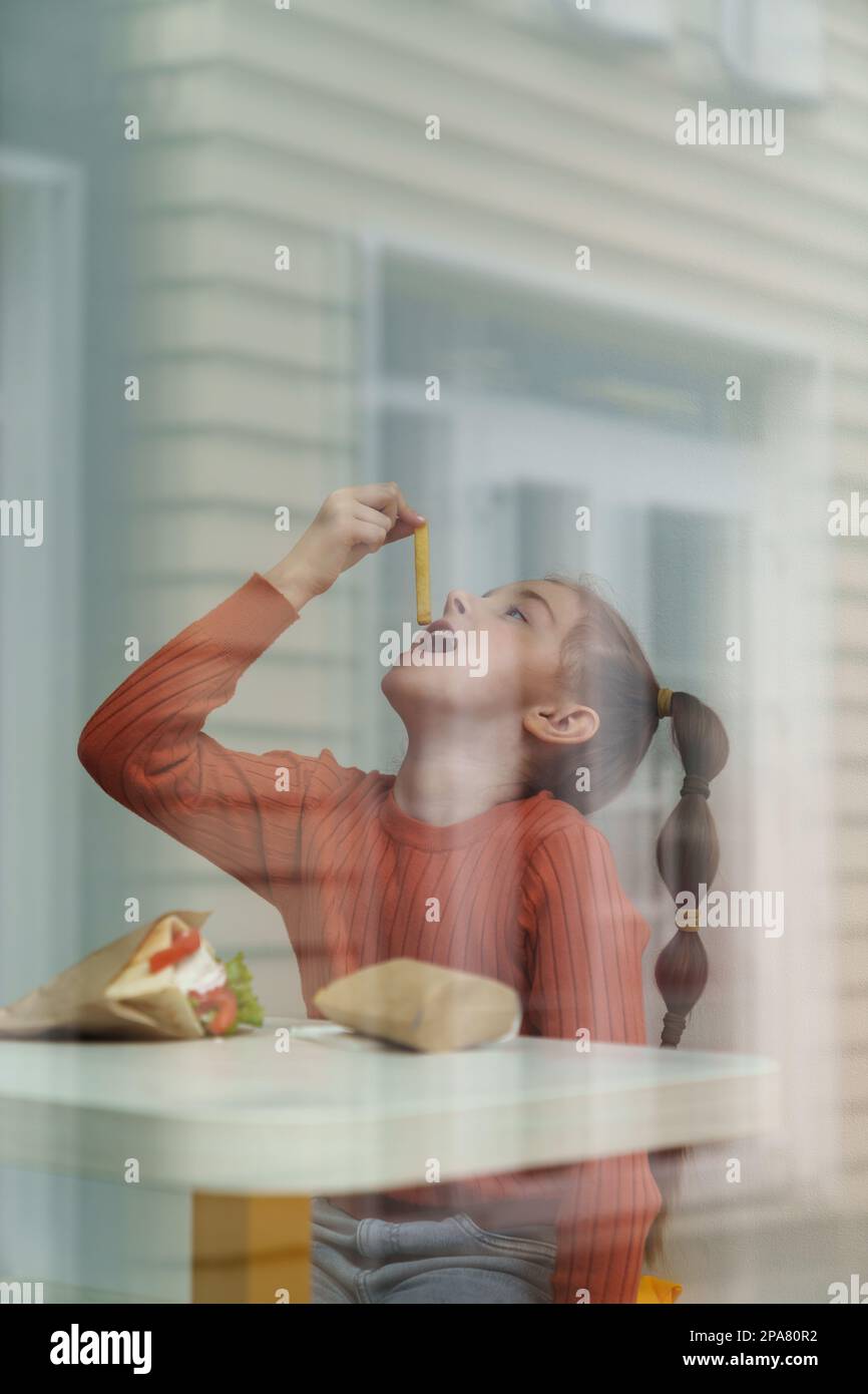 Hungry little girl eats fries in a restaurant. Cute white kid eating ...