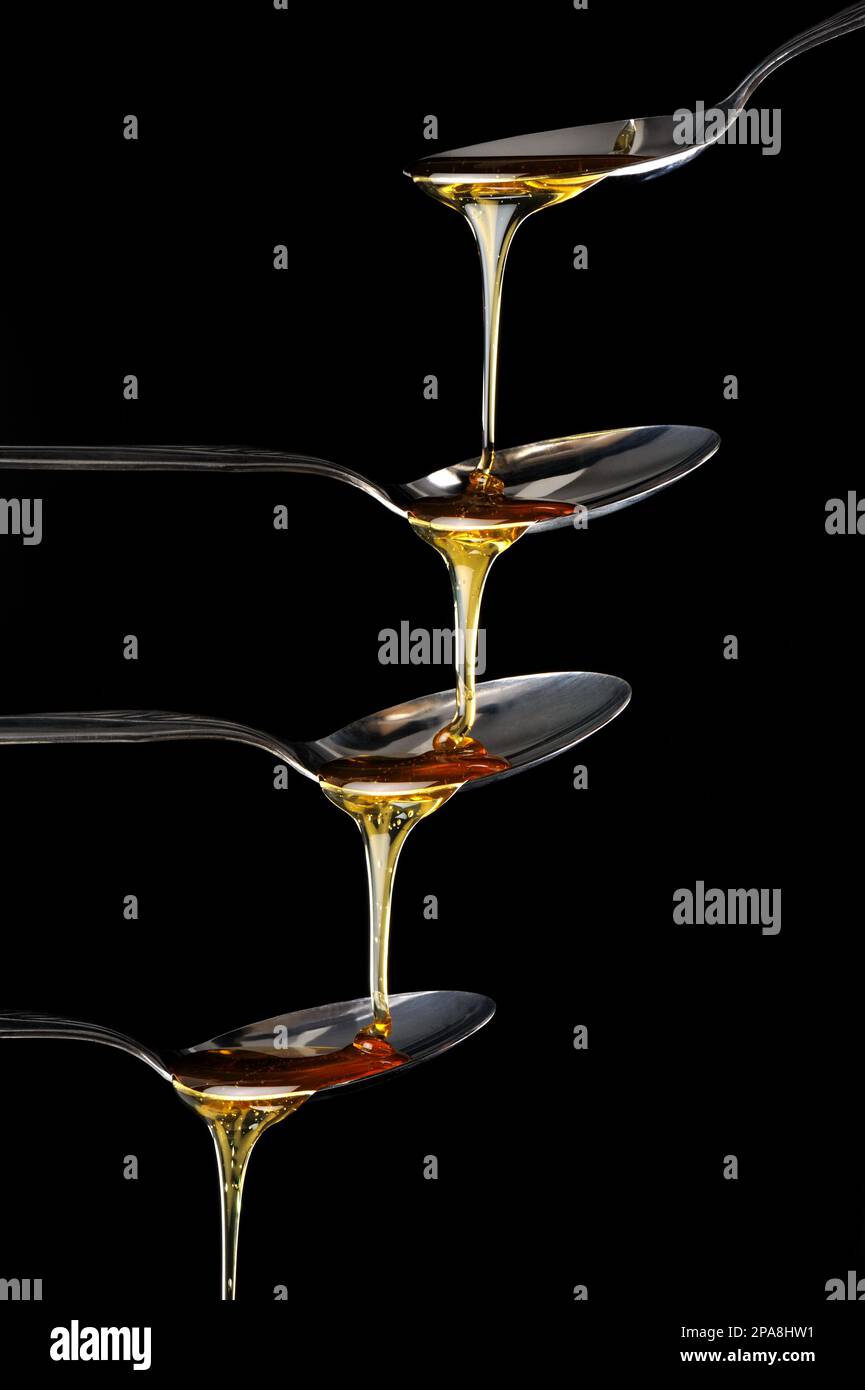 honey flowing from stacked steel spoons Stock Photo - Alamy