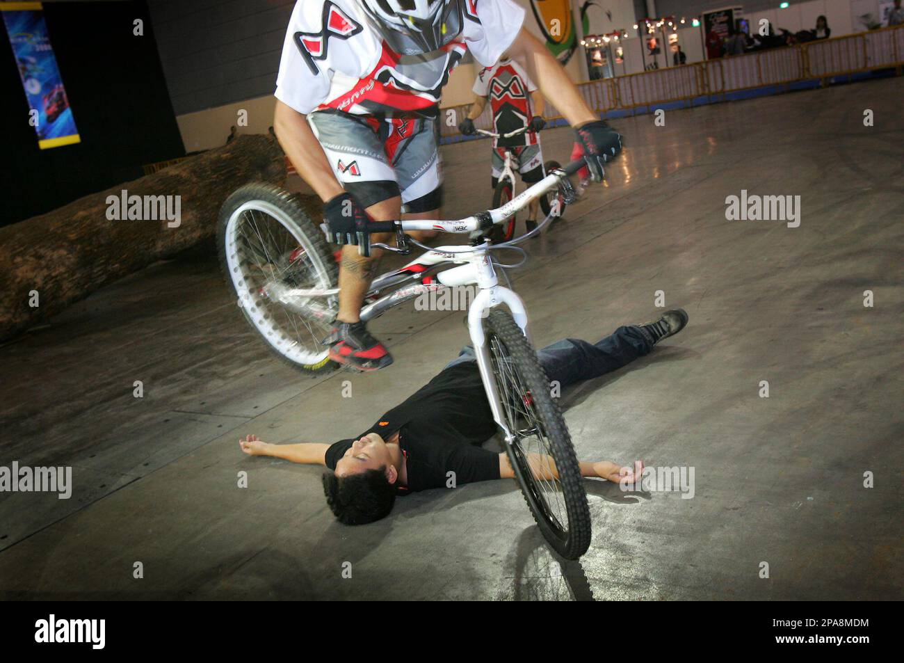 A trial biker performs a stunt by jumping over two people laying on the ...