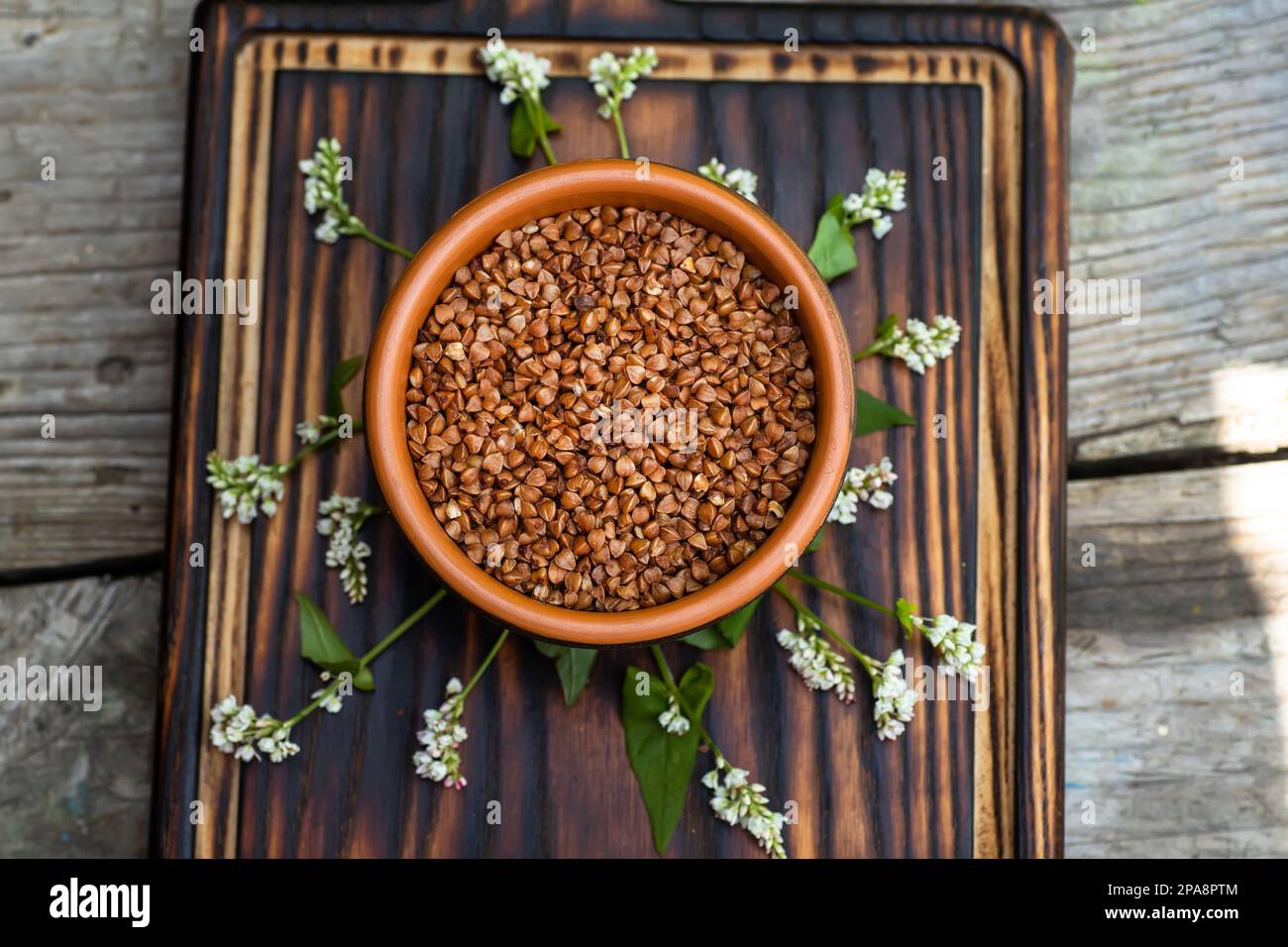 Dry buckwheat in a clay brown plate. Top view of a cutting wooden board ...