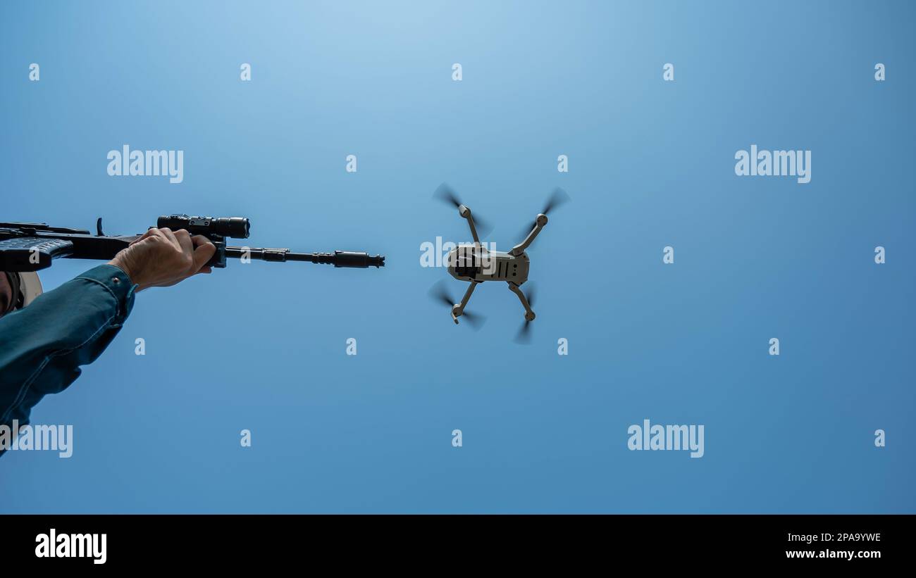 A man aims to shoot a rifle at a flying drone against a blue sky Stock ...