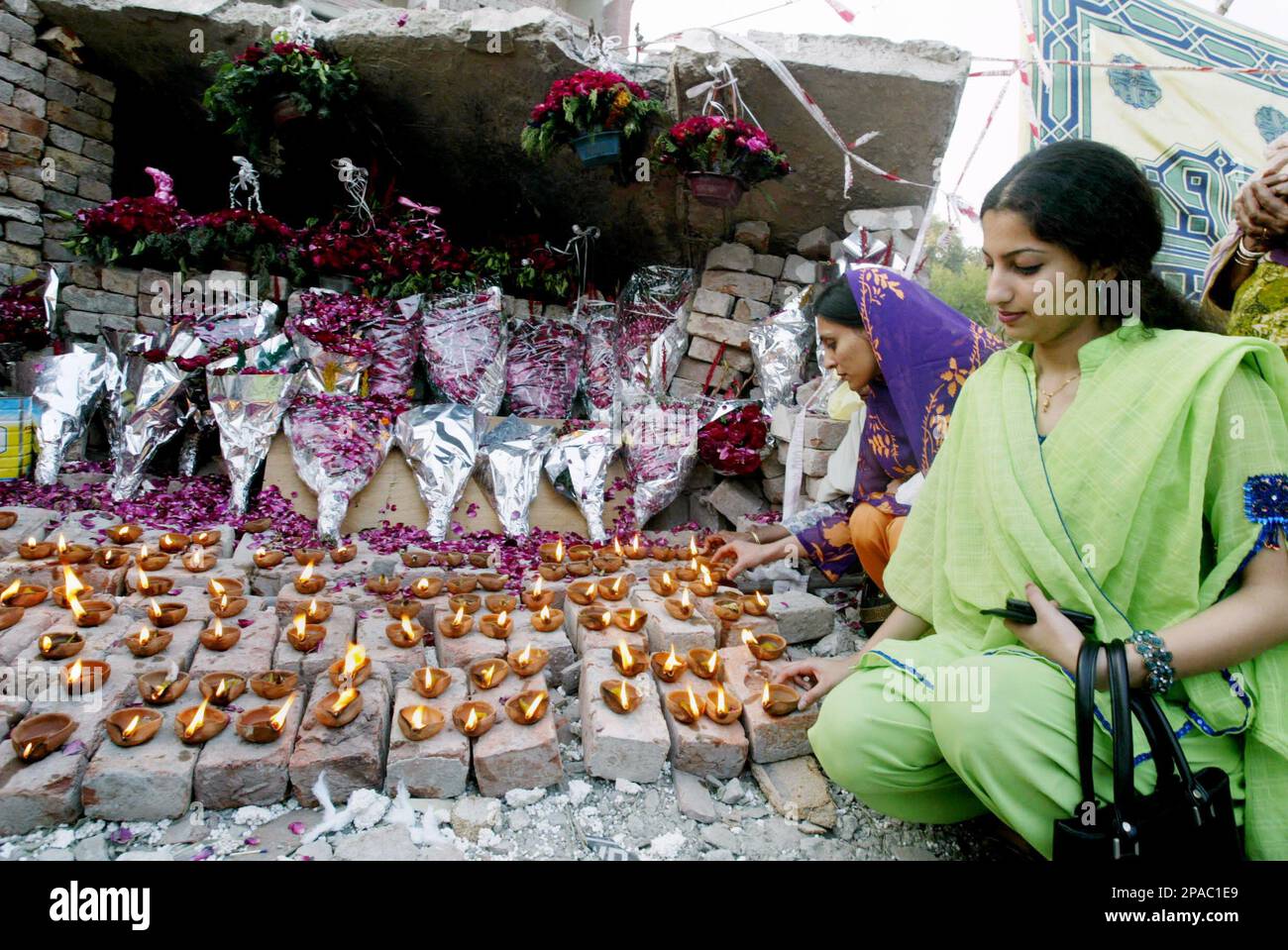 Pakistani women light oil lamps after placing the flower bouquet to pay ...