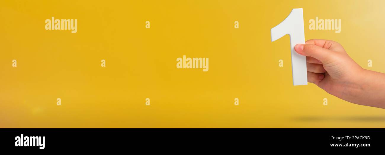 Number one in hand. A hand holds a white number one on a yellow ...