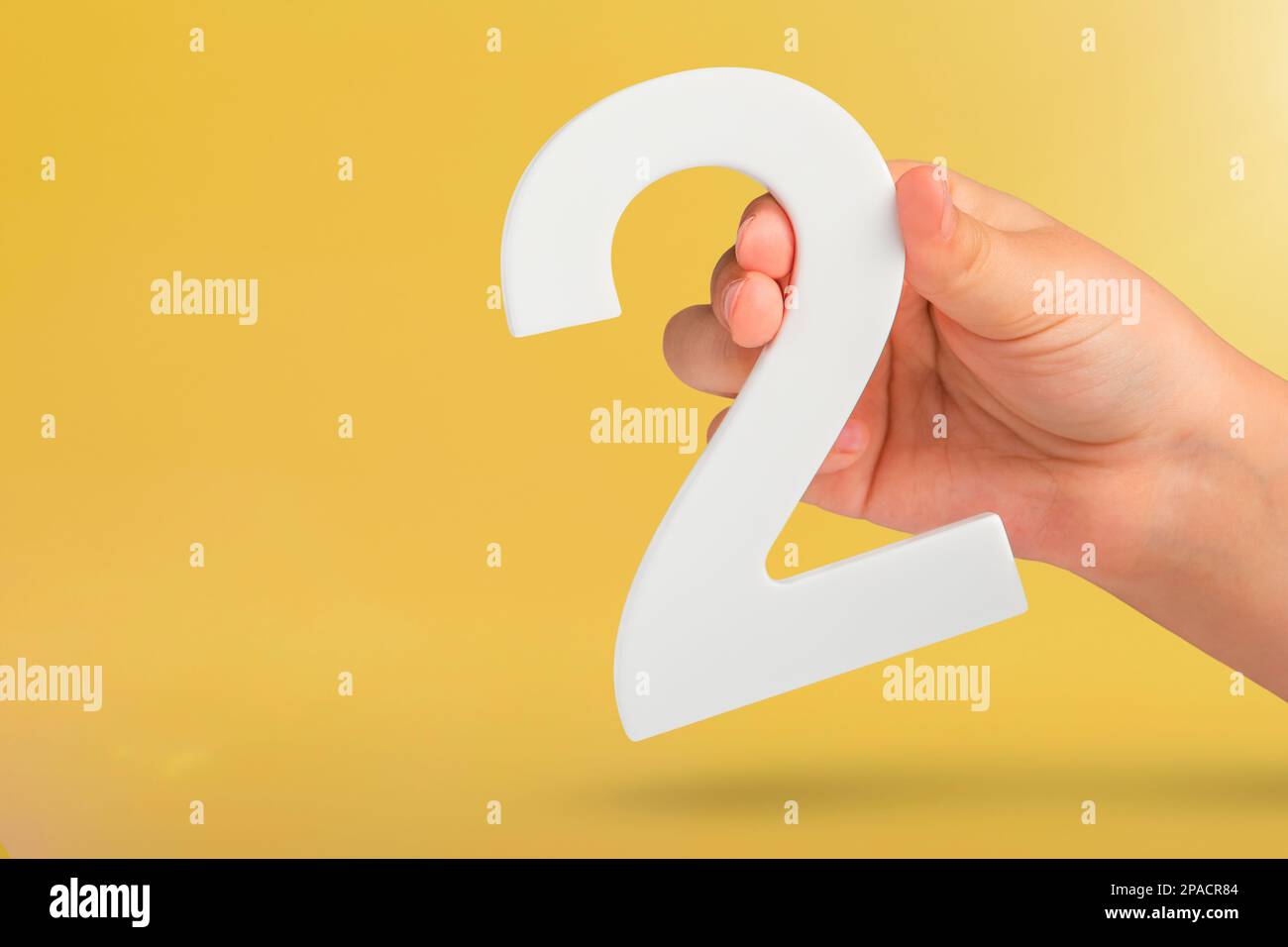 Number two in hand. Hand holding white number 2 on yellow background ...