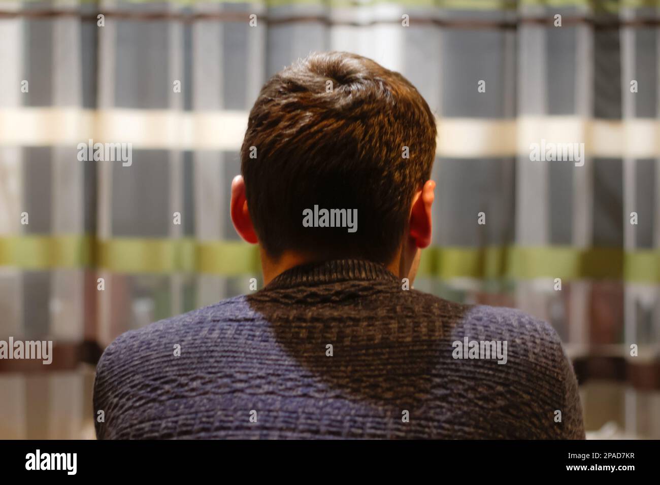 Back view of young man sitting home and thinking. Lost in thoughts ...