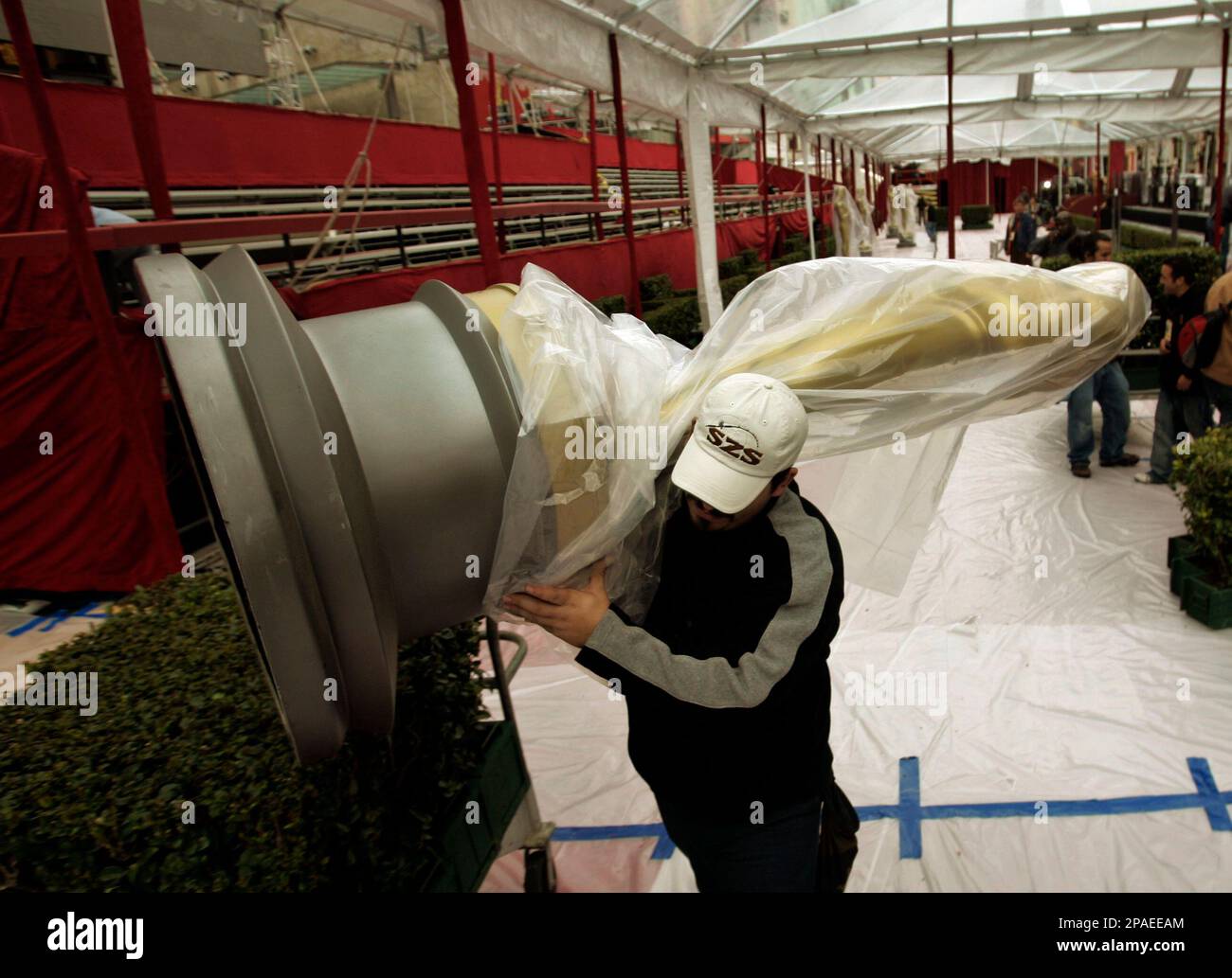 A worker carries an Oscar statue, wrapped in plastic to protect it from ...