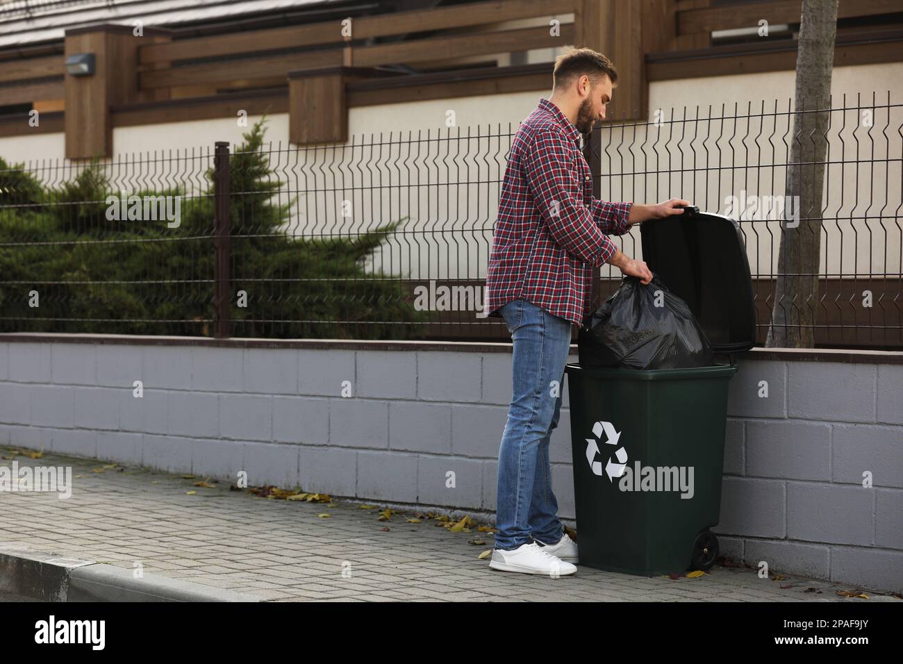 Man putting garbage bag into recycling bin outdoors Stock Photo - Alamy