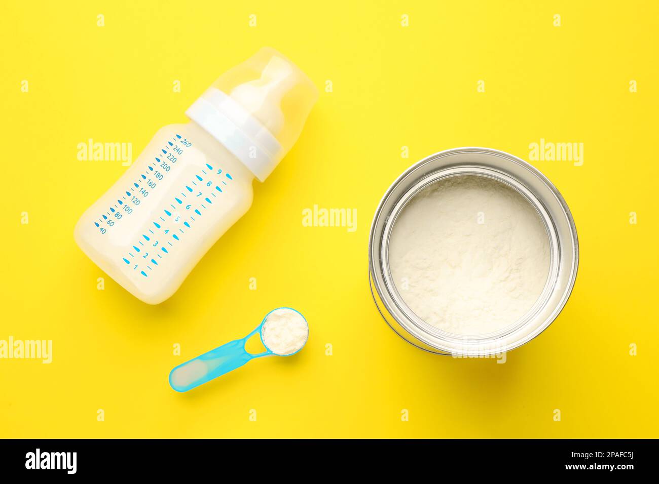 Feeding bottle with infant formula and powder on yellow background ...
