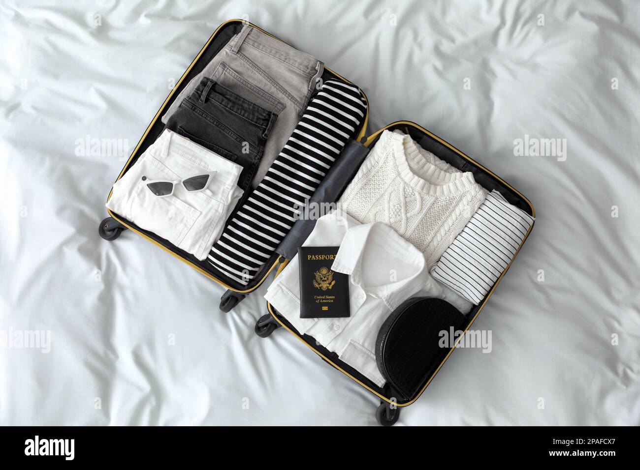 Open suitcase with clothes, passport and accessories on bed, top view ...