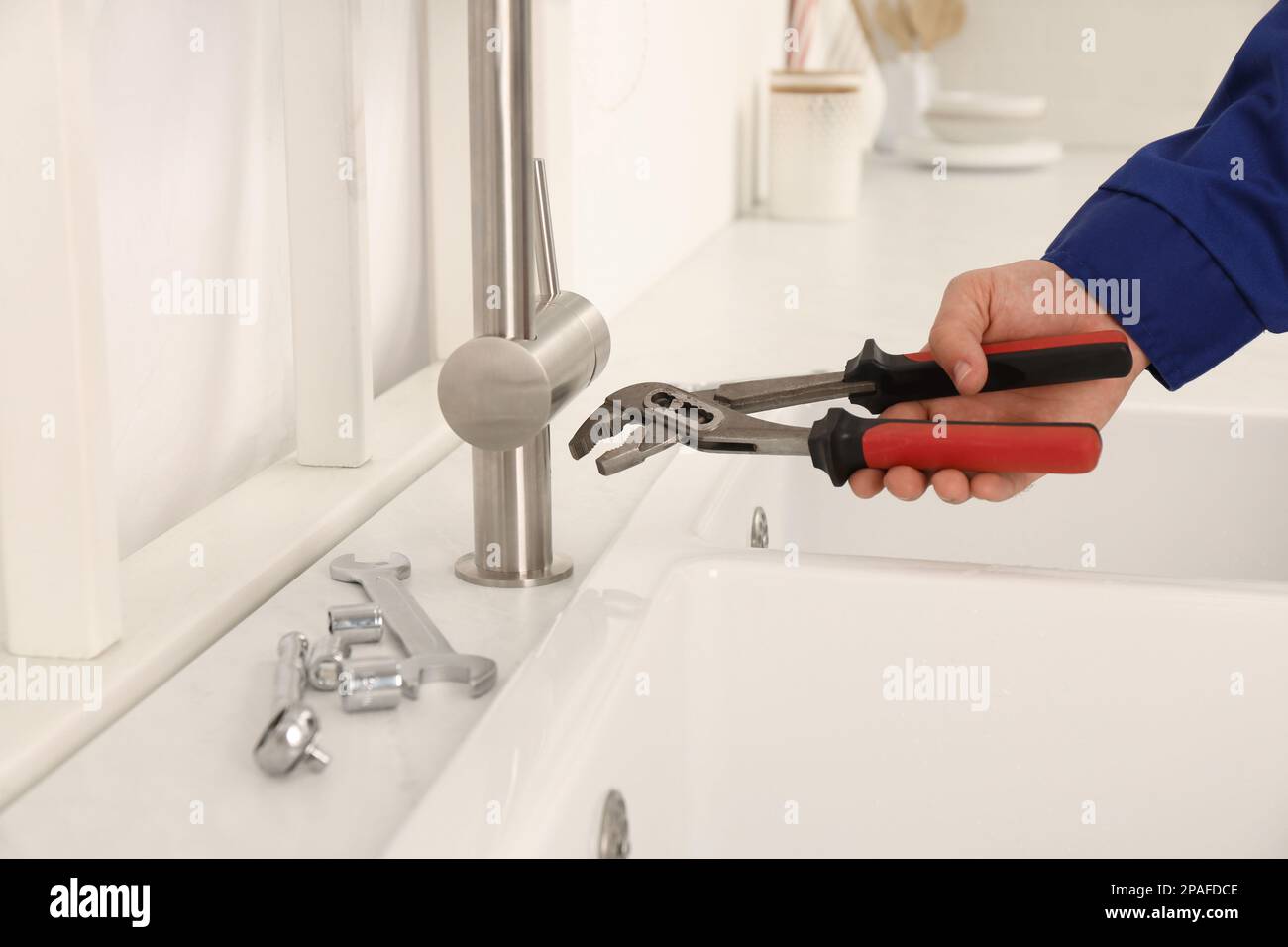 Plumber with spanner near sink in kitchen, closeup. Water tap ...