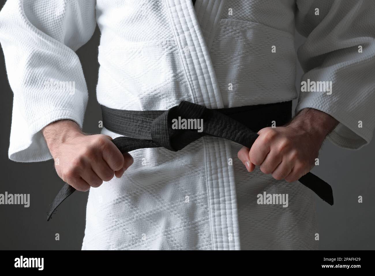 Karate coach wearing kimono and black belt on grey background, closeup ...