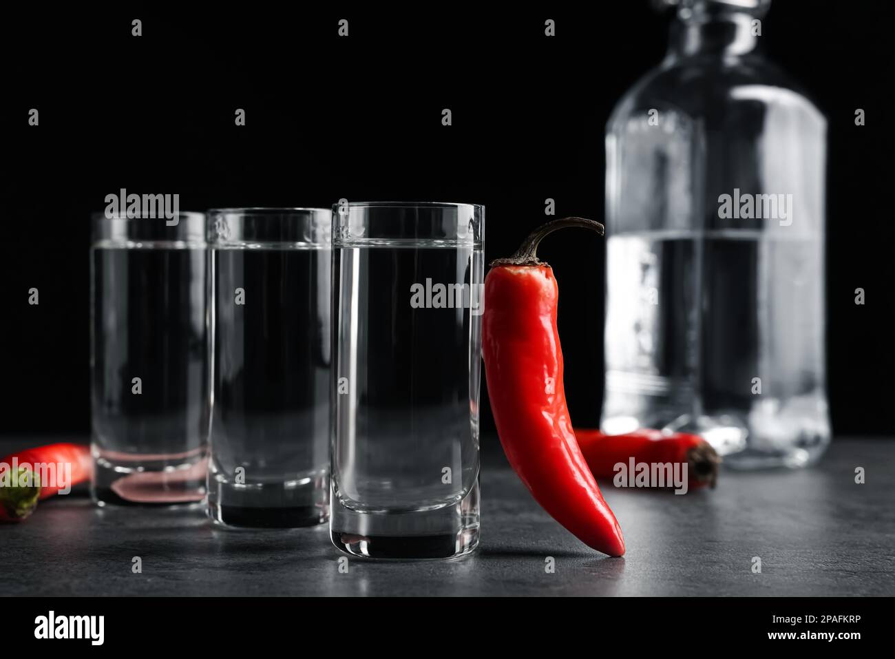 Red hot chili peppers and vodka on grey table against black background ...
