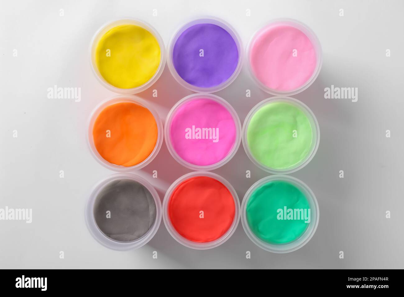 Plastic containers with different color play dough on white background ...