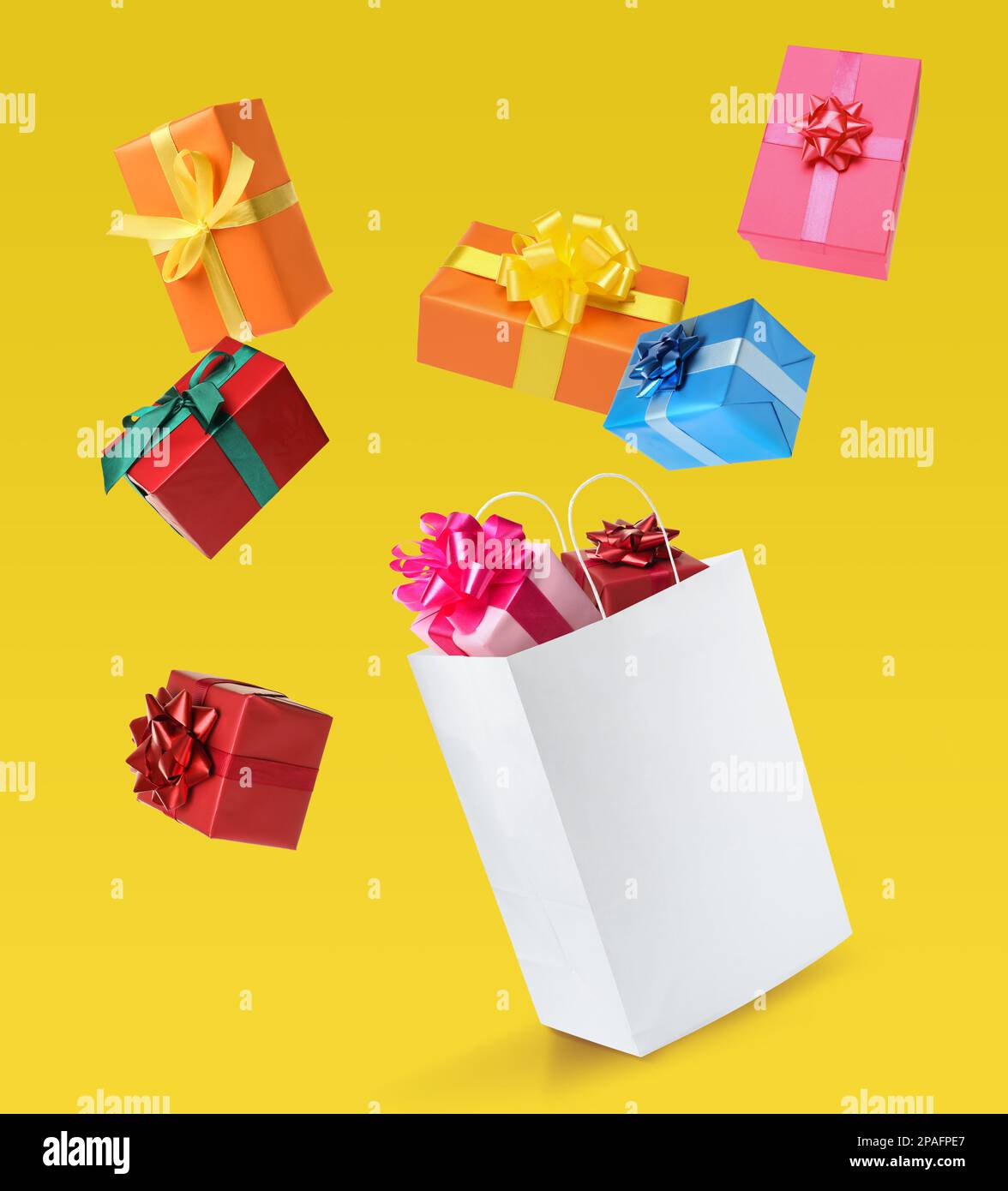 Many different gift boxes falling into paper shopping bag on yellow ...