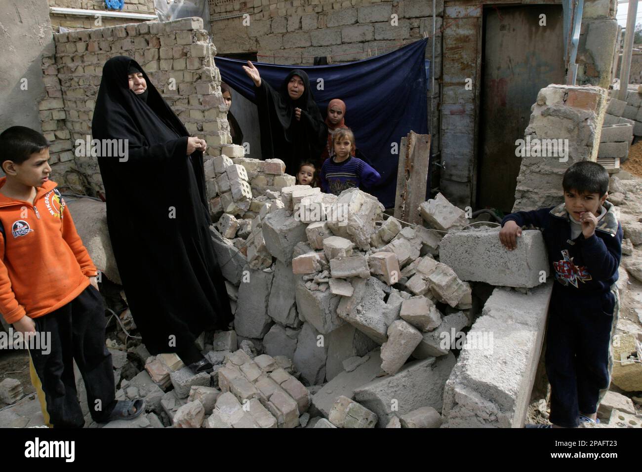 Iraqis stand by a wall brought down during an overnight US troops raid ...