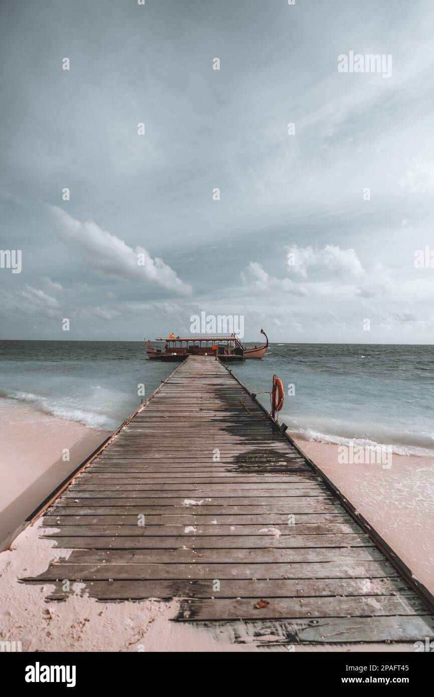 A vertical shot of a very long wooden pier on a Maldivian beach island ...