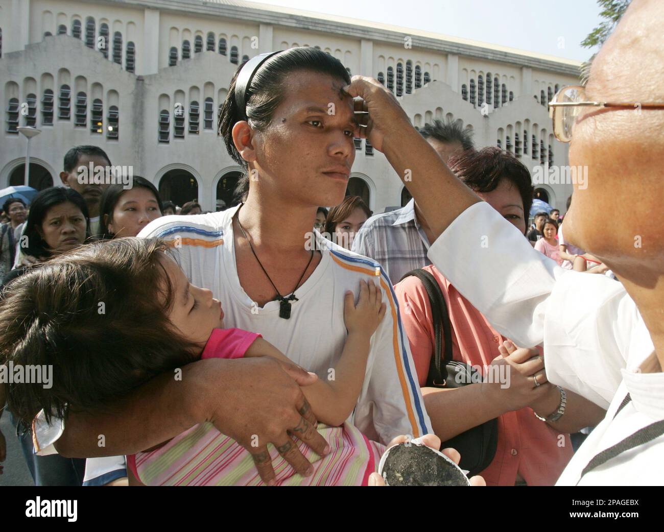 A Catholic priest applies ash on the forehead of a father on Ash ...