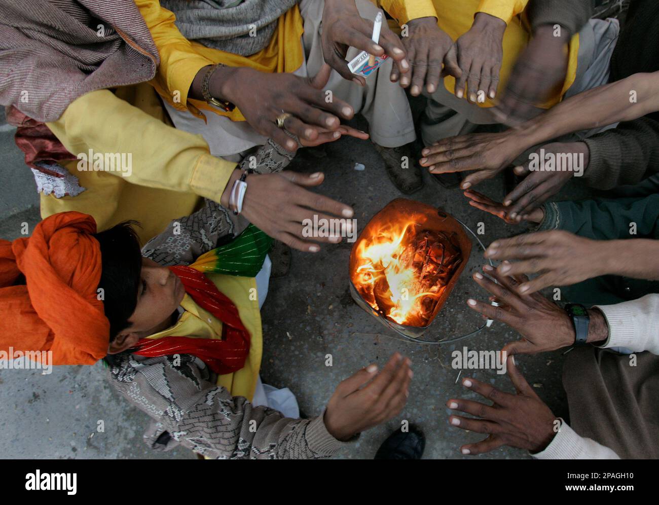 Pakistani street performers sit around a fire during a chilly evening ...