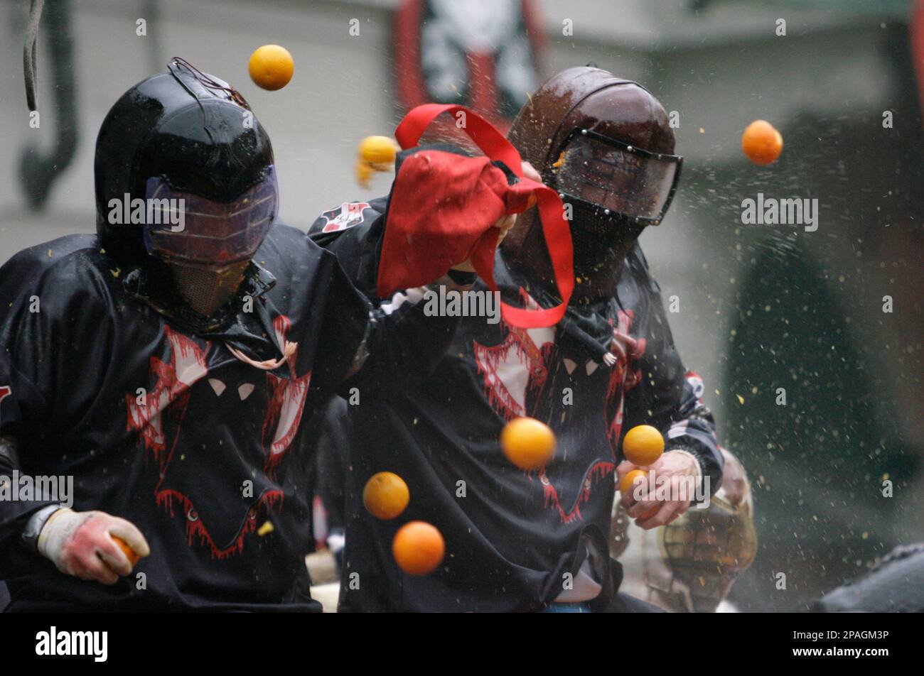 People wearing protection helmets and costumes throw oranges as part of ...
