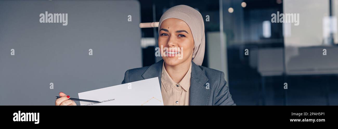 Smiling muslim businesswoman in hijab shows a graph of company's profit ...