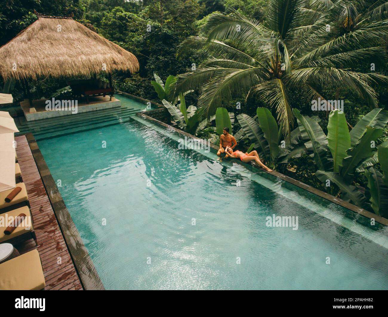 Aerial shot of man and woman relaxing at the poolside. Couple enjoying ...